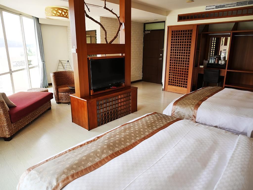 Quarto de hotel com duas camas, televisão, área de estar e guarda-roupa.
