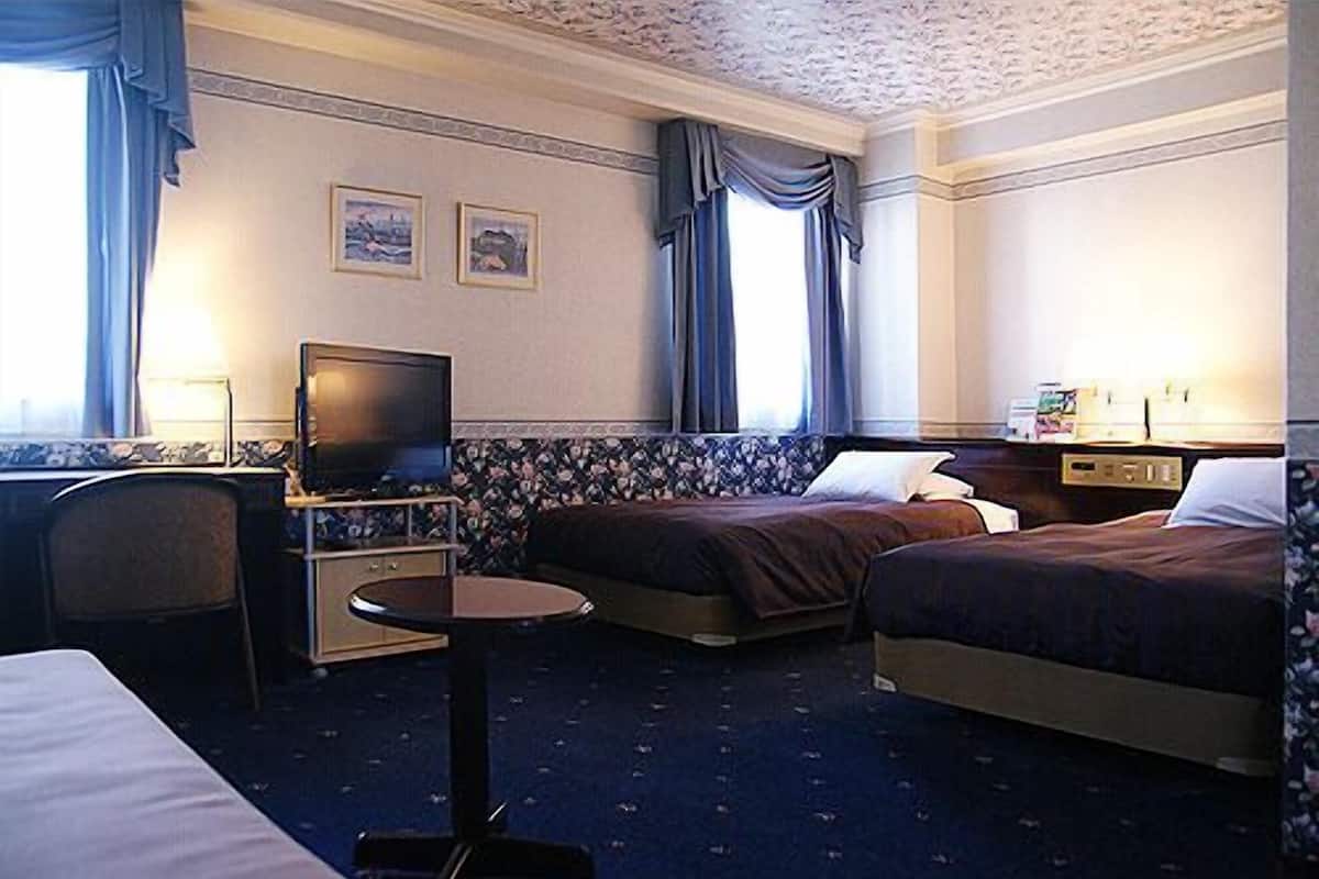 Quarto de hotel com duas camas, televisão, escrivaninha e uma mesinha redonda.