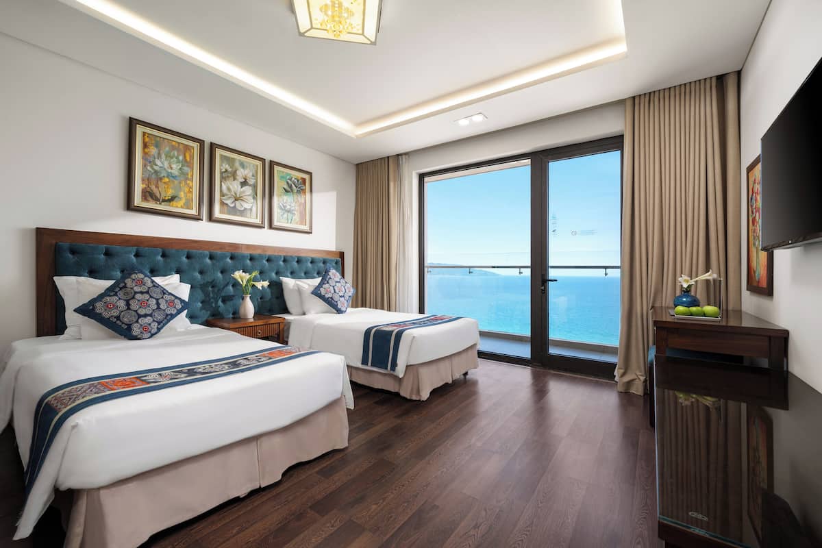 Quarto de hotel com duas camas, uma janela grande com vista para o mar e obras de arte na parede.