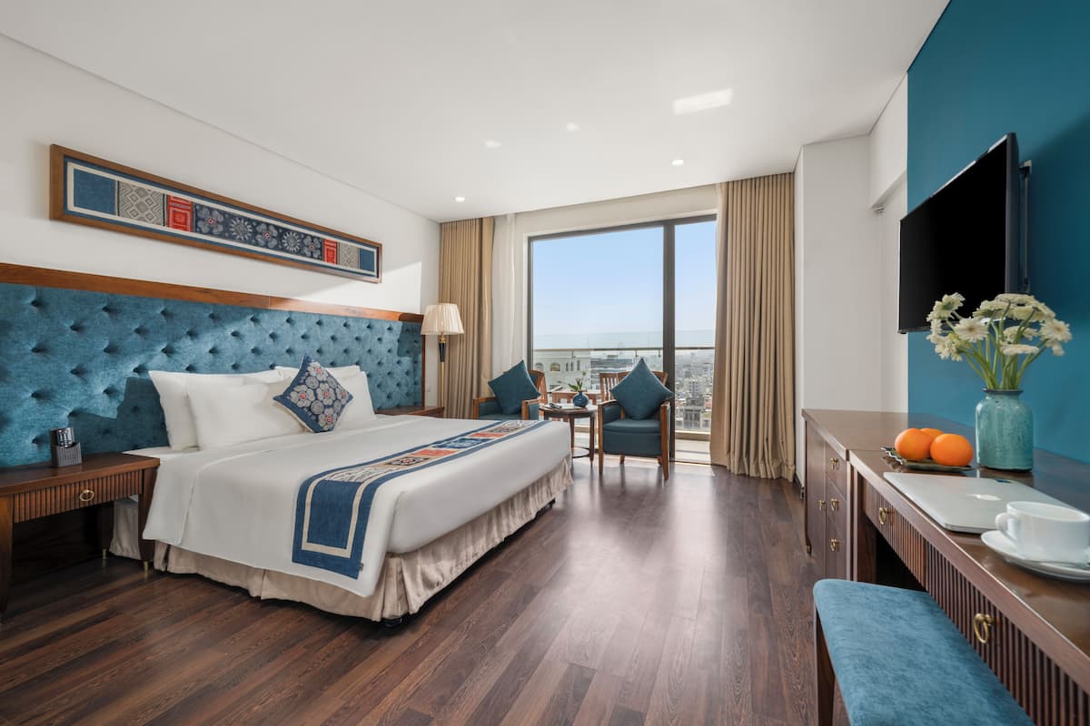 Quarto de hotel com uma cama grande, uma escrivaninha, uma cadeira e vista para a cidade.