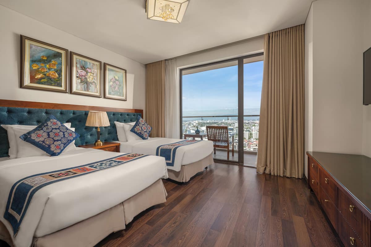 Quarto de hotel com duas camas, uma janela grande com vista para a cidade e uma varanda com uma cadeira.