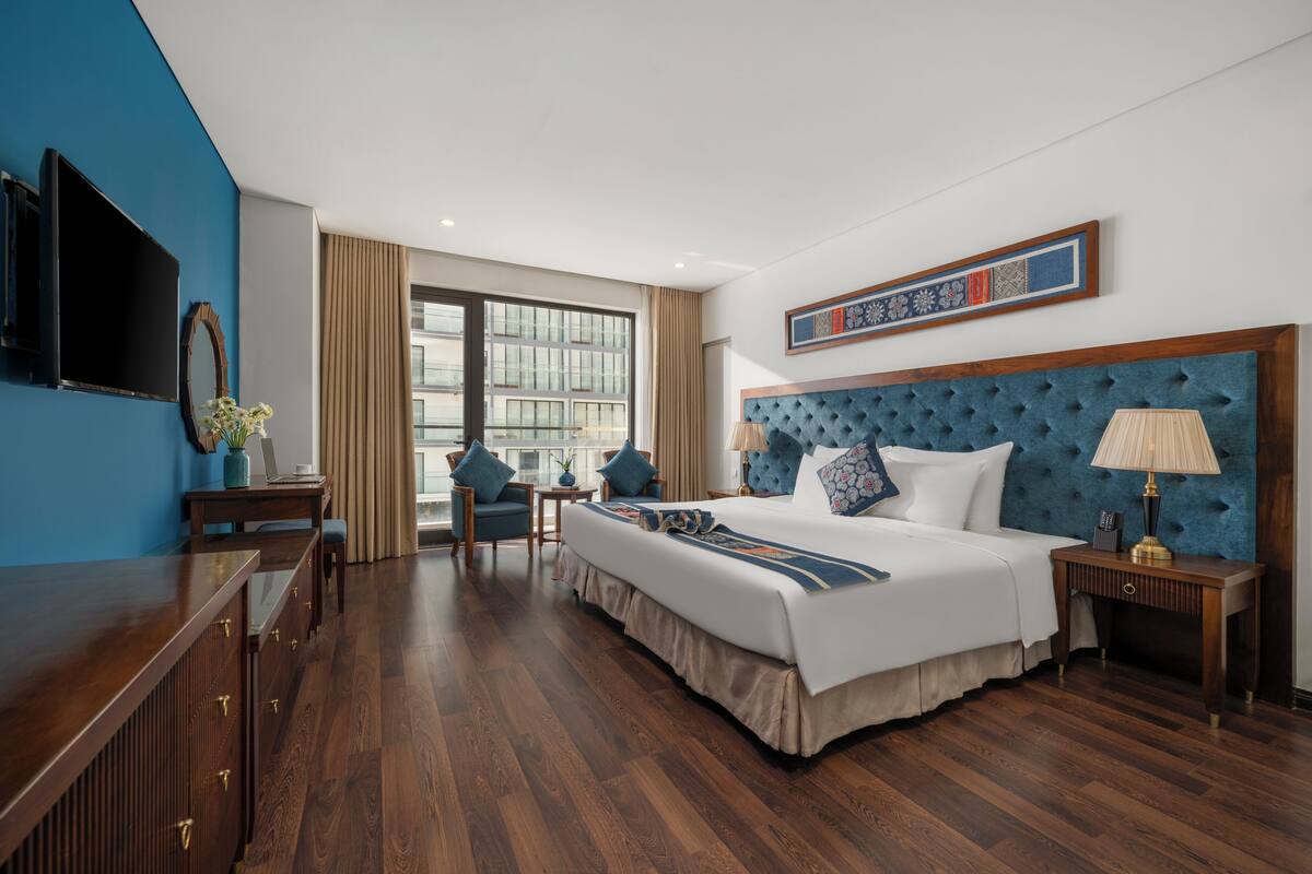 Quarto de hotel com cama grande, escrivaninha, cadeira e televisão.