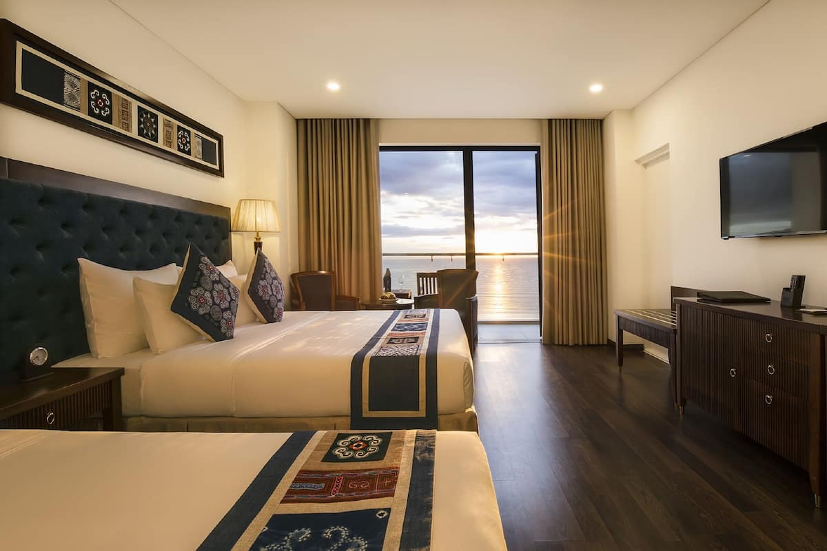 Quarto de hotel com cama grande, televisão, escrivaninha e vista para o mar.