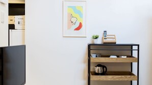 Uma sala de estar moderna com televisão de tela plana, uma pintura abstrata emoldurada, uma prateleira de madeira com uma cafeteira e um controle remoto.
