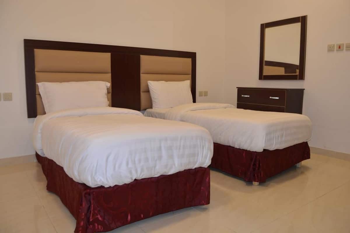 Quarto de hotel com duas camas, cabeceira de madeira, um espelho e uma cômoda pequena.