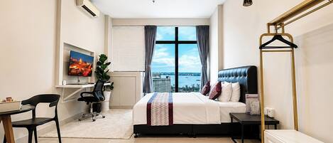 Quarto de hotel moderno com cama, escrivaninha, cadeira e uma janela ampla com vista para a cidade.