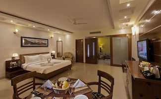 Quarto de hotel com cama, mesa de jantar com frutas, televisão e espelho.