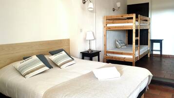 Quarto de hotel com uma cama grande, duas almofadas, uma luminária de cabeceira, uma beliche de madeira e uma mesa pequena.