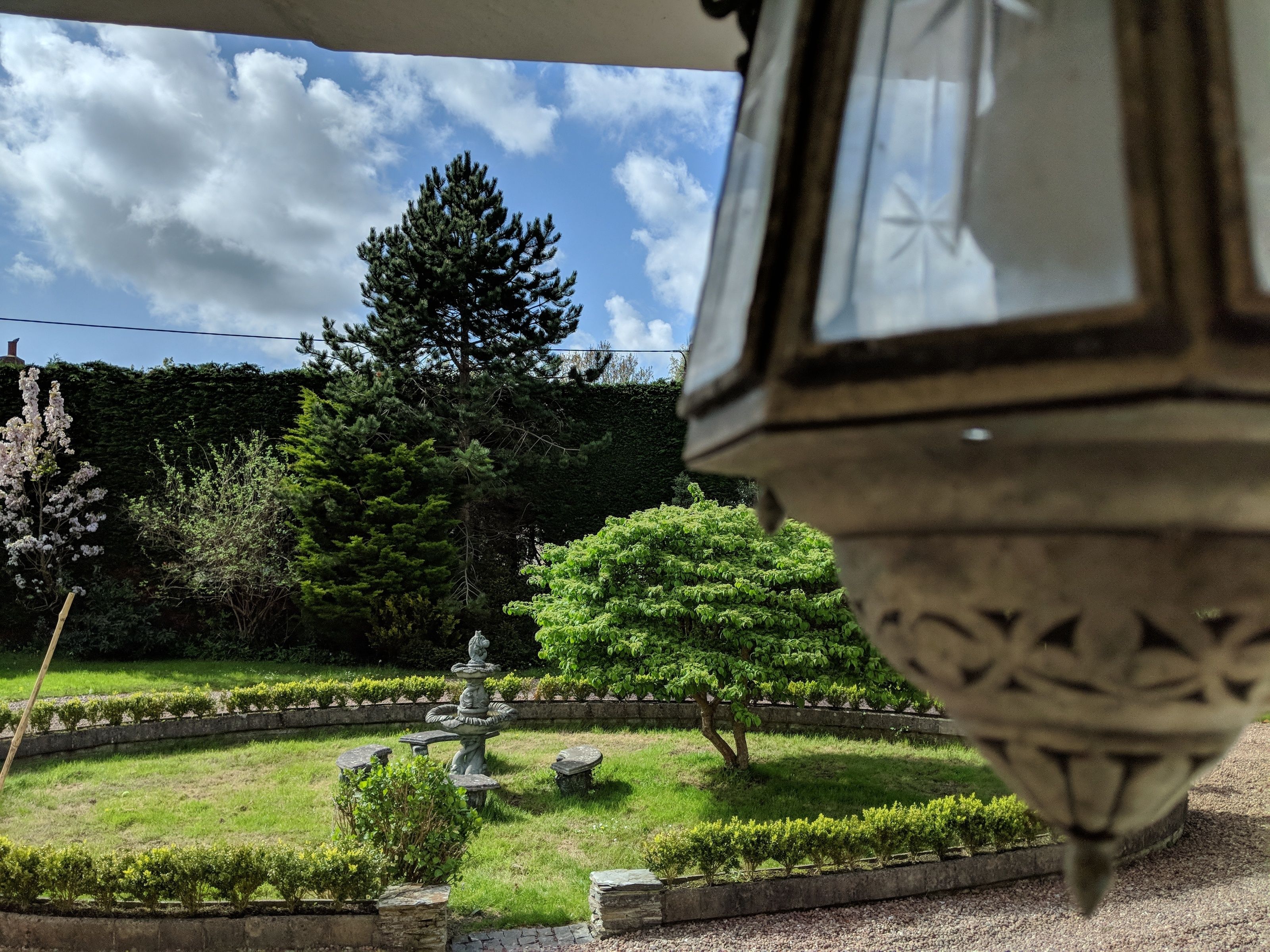 Um jardim com uma fonte de pedra, sebes bem aparadas e diversas árvores.