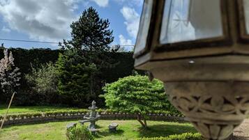 Um jardim com uma fonte de pedra, sebes bem aparadas e diversas árvores.