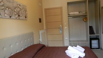 Quarto de hotel com uma cama, radiador, guarda-roupa e um quadro na parede.
