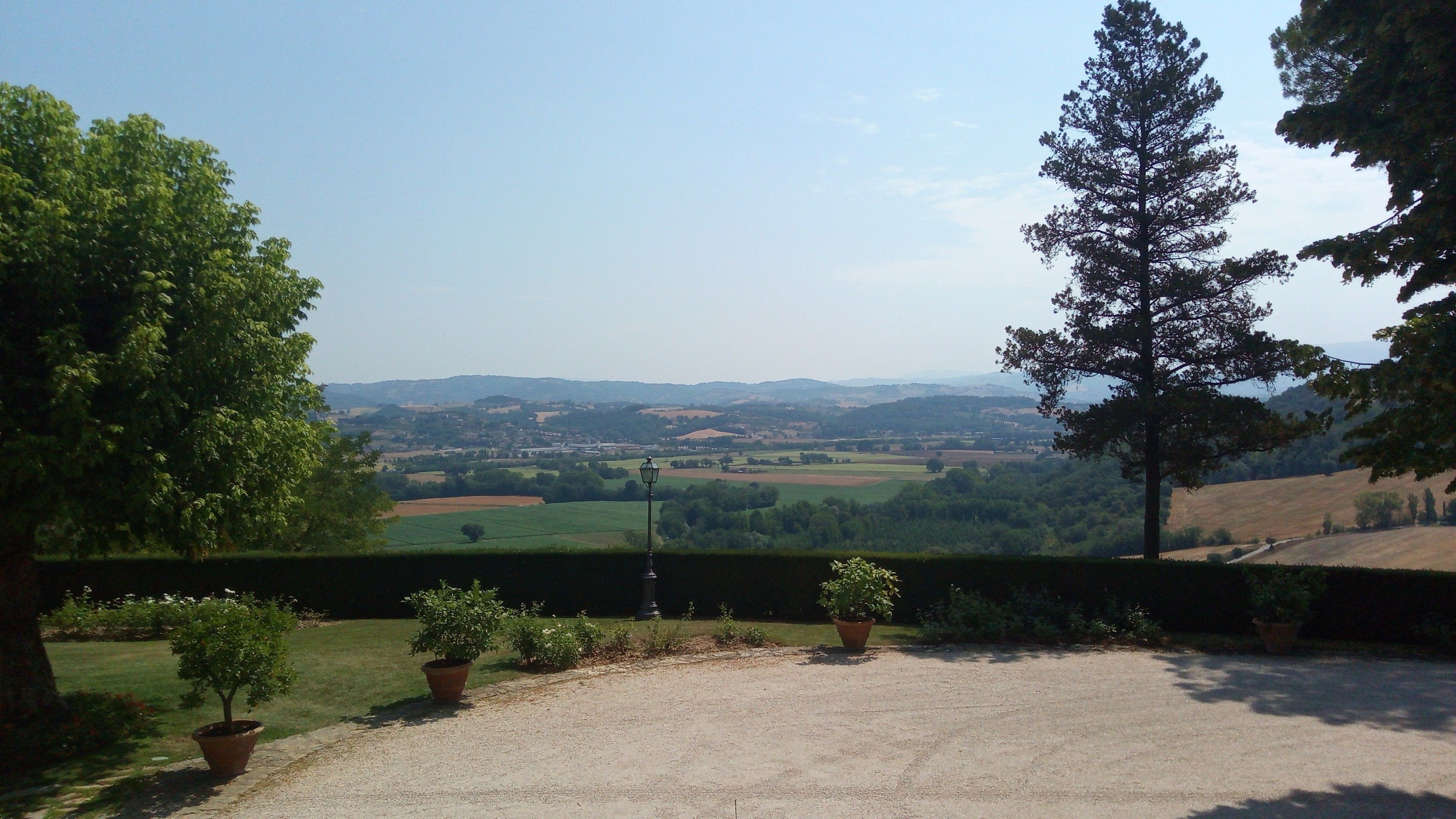 Uma entrada de cascalho leva a uma casa com vista para uma paisagem rural, com campos e colinas ao longe.