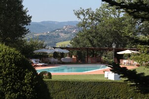 Área de piscina com espreguiçadeiras e guarda-sóis, cercada por vegetação e vista para colinas ao longe.