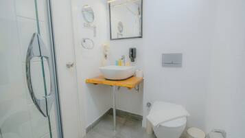 Casa de banho com cabine de duche em vidro, lavatório branco com bancada de madeira, sanita e espelho com luzes por cima.