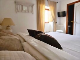 Quarto de hotel com cama, luminária, cortinas, televisão na parede e uma porta.