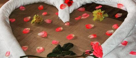 Arranjo em formato de coração com tecido branco, pétalas de rosa e um ramo de rosa.