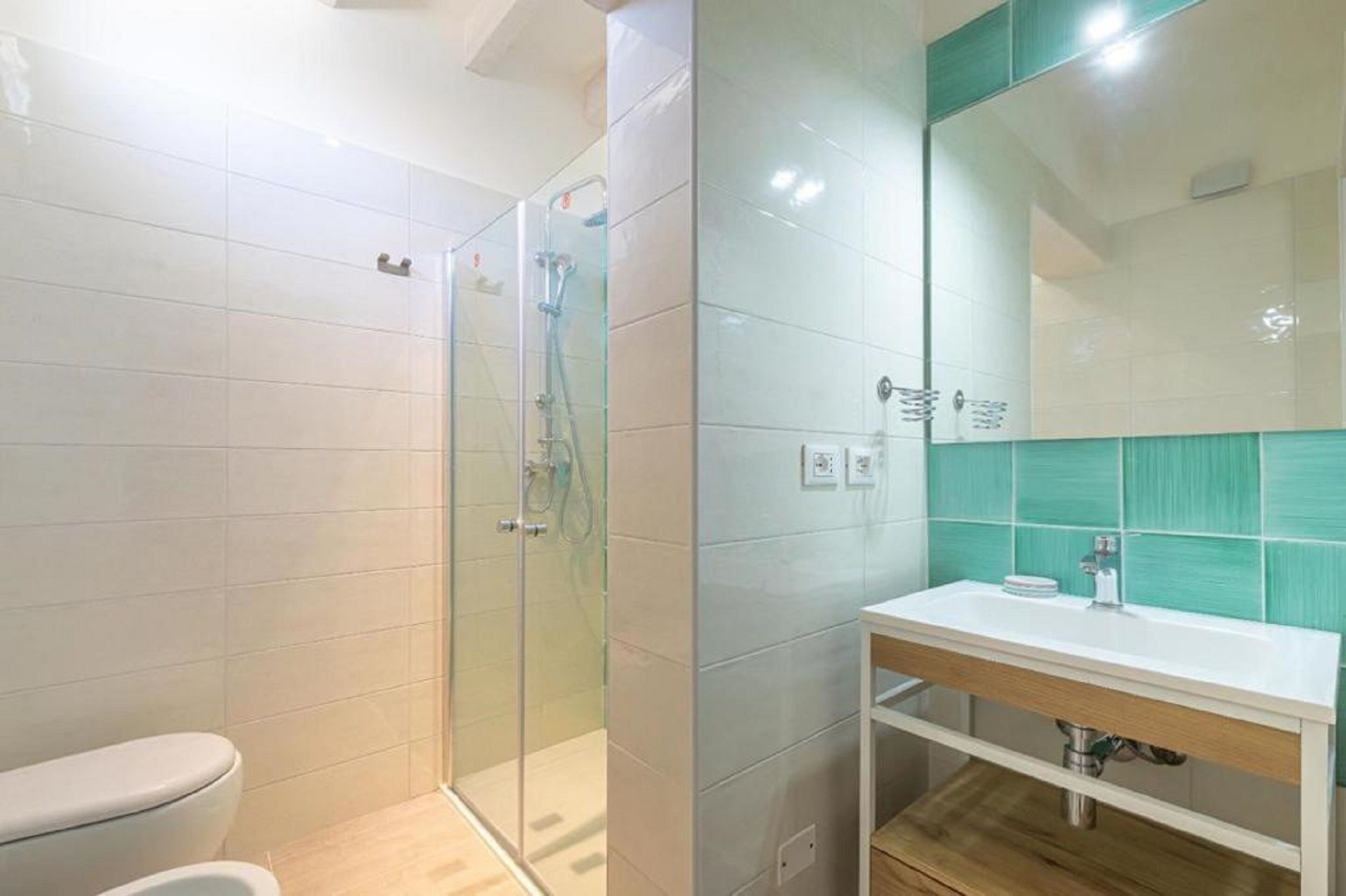 Uma casa de banho moderna com chuveiro em cabine de vidro, lavatório branco e um espelho grande.