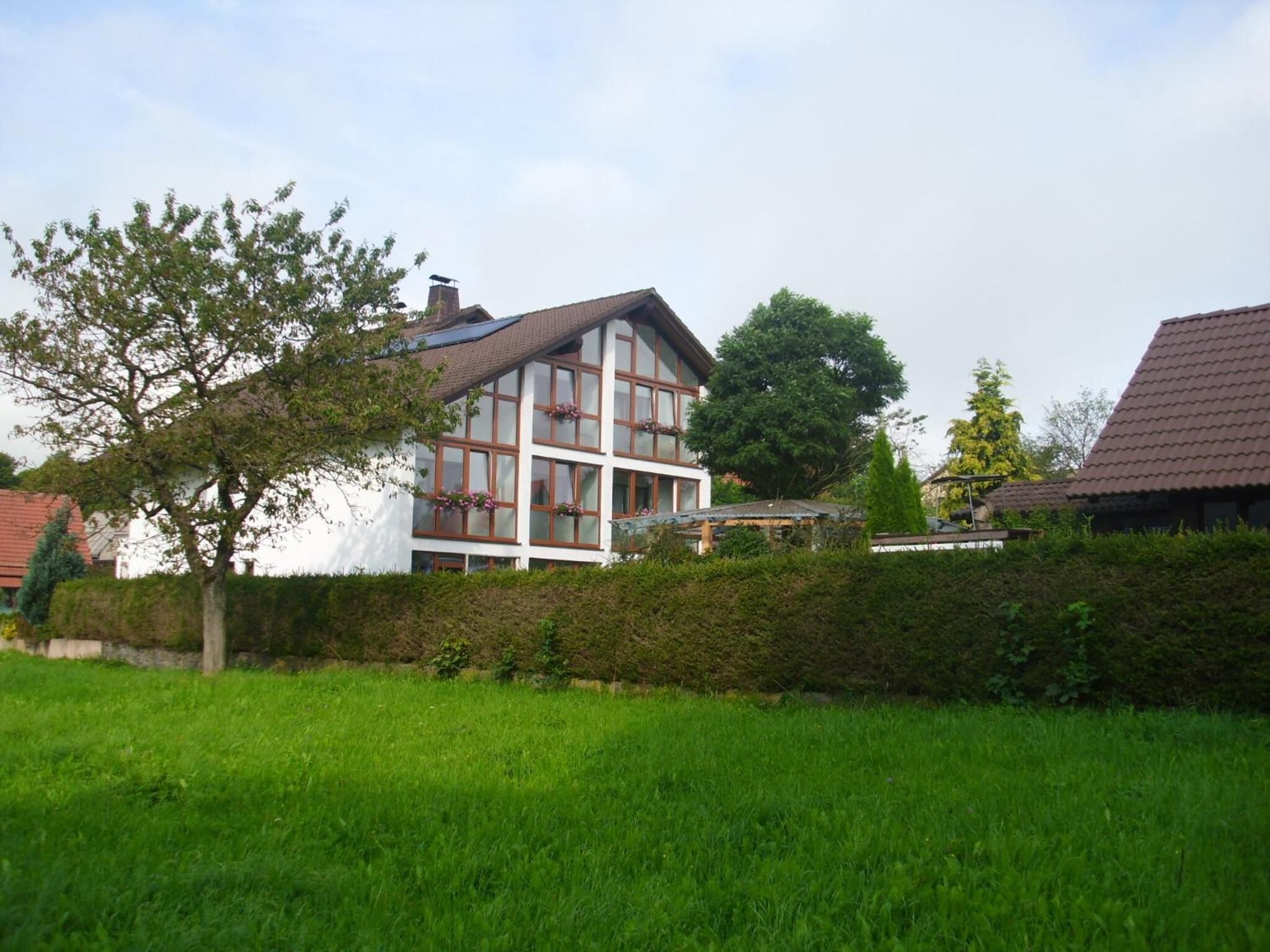 Uma casa de dois andares com telhado inclinado, janelas amplas e um jardim em primeiro plano.