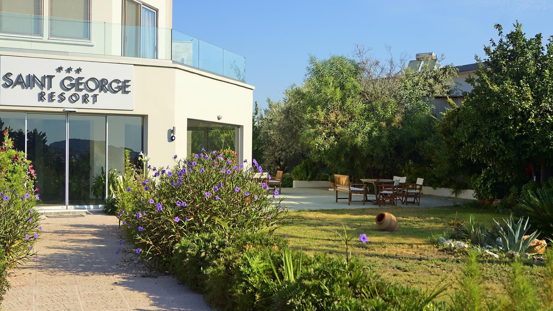 Resort Saint George, com um caminho livre que leva à entrada, rodeado por vegetação exuberante e uma área de pátio com mobiliário externo.