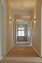 Um corredor comprido e estreito com pisos e paredes revestidas de carpete, que leva a um quarto com janela e radiador.