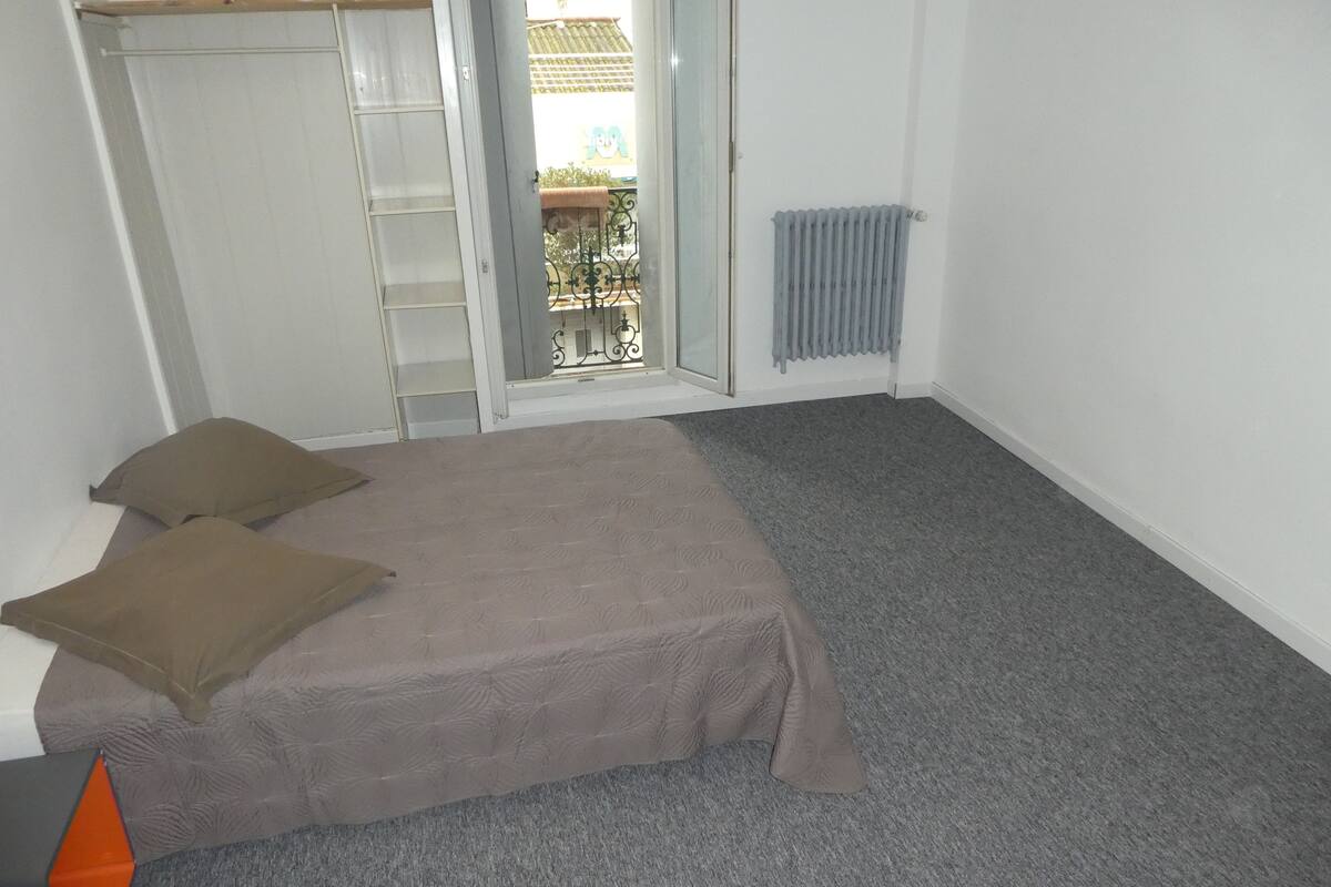 Quarto com cama, duas almofadas, radiador e porta de vidro deslizante para uma varanda.