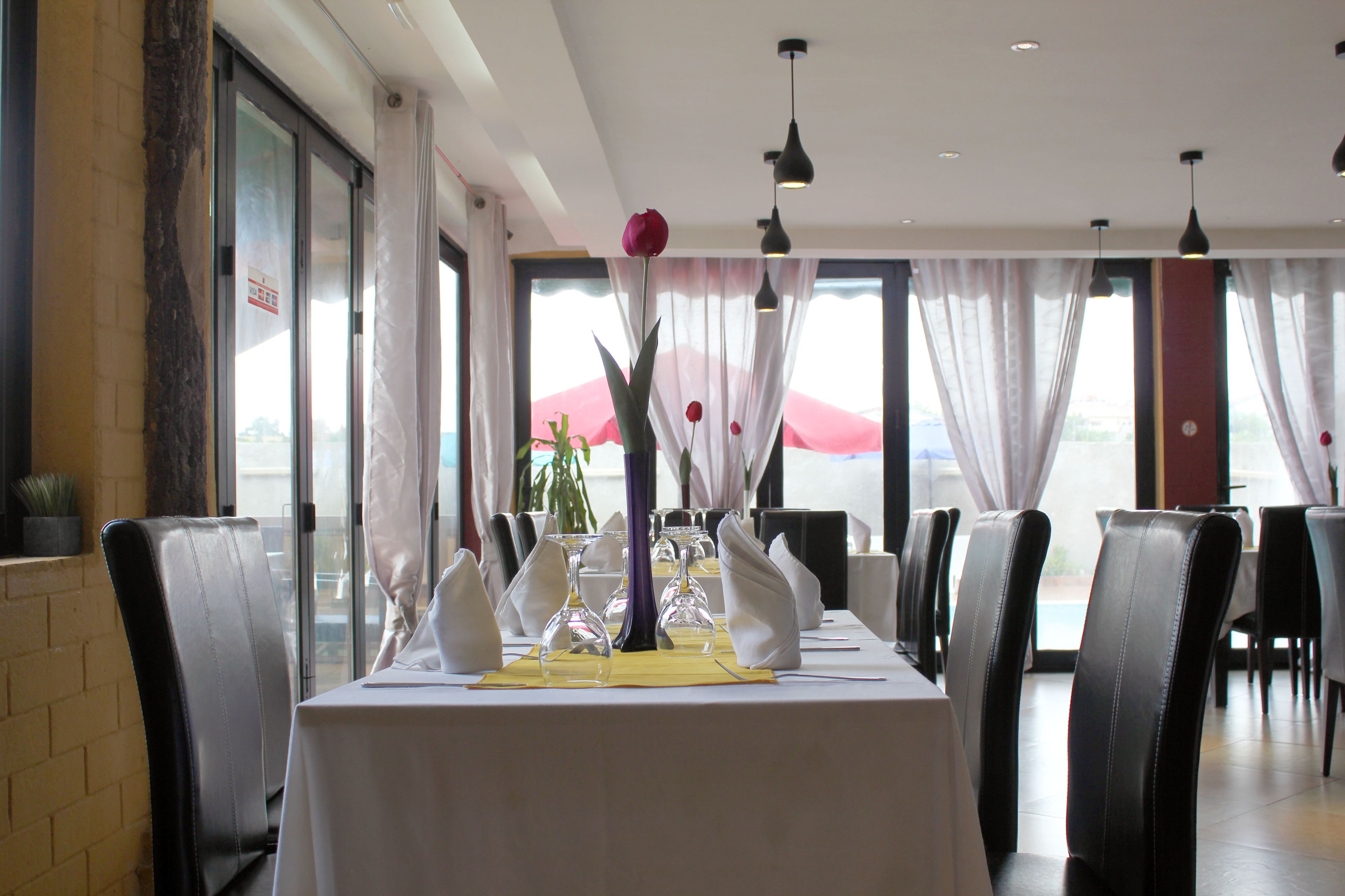 Restaurante com uma mesa comprida posta para refeição, com cadeiras de couro preto e toalha de mesa branca.