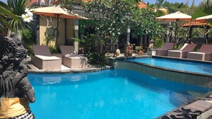 Piscina com espreguiçadeiras e guarda-sóis, cercada por plantas tropicais e uma estátua decorativa.