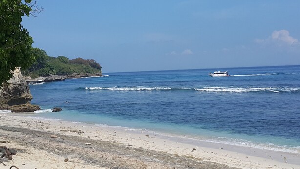 Uma praia com águas azuis cristalinas, um barco e falésias rochosas.