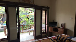 Quarto de hotel com cama, televisão, escrivaninha e varanda com vista para o verde.