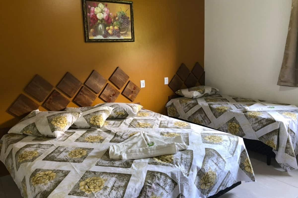 Quarto com duas camas, cada uma com colcha de padrão floral e cabeceiras de madeira.