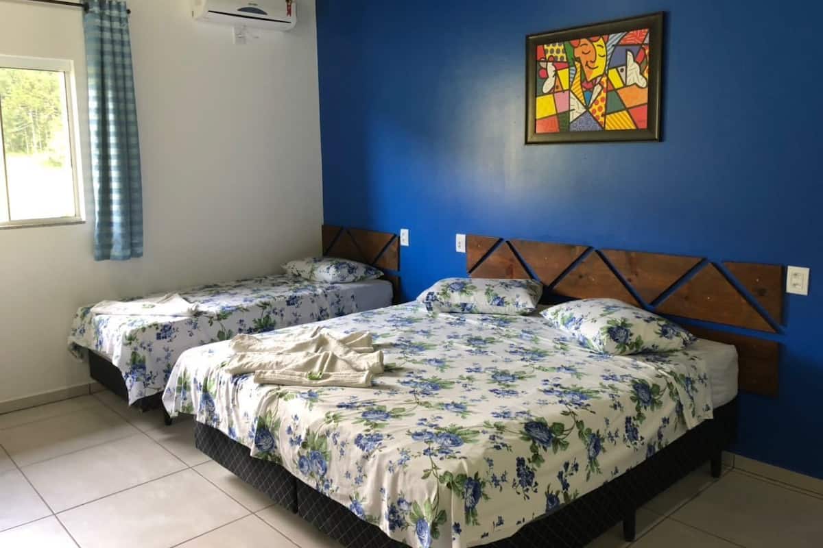 Quarto com duas camas, parede azul e uma pintura abstrata colorida.