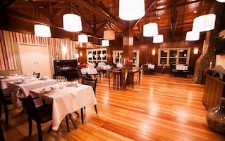 Restaurante com interiores em madeira, várias mesas e luminárias pendentes.