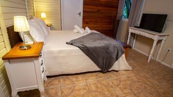 Cama bem arrumada com manta cinza, abajur e mesa de cabeceira de madeira.