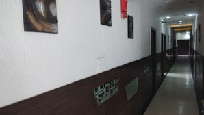 Um corredor com parede branca, rodapé castanho e alarme de incêndio vermelho.