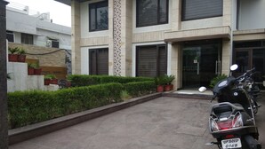 Um edifício moderno com entrada pavimentada, uma motocicleta estacionada em frente e plantas em vasos ao longo do caminho.
