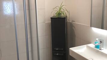 Uma casa de banho moderna com cabine de duche em vidro, um armário preto alto e uma sanita branca com espelho em cima.