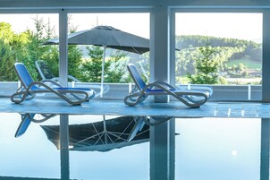 Área da piscina com espreguiçadeiras e um guarda-sol, com vista para uma paisagem deslumbrante.