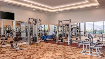 Uma academia ampla com diversos equipamentos de exercício, um espelho grande e uma televisão na parede.