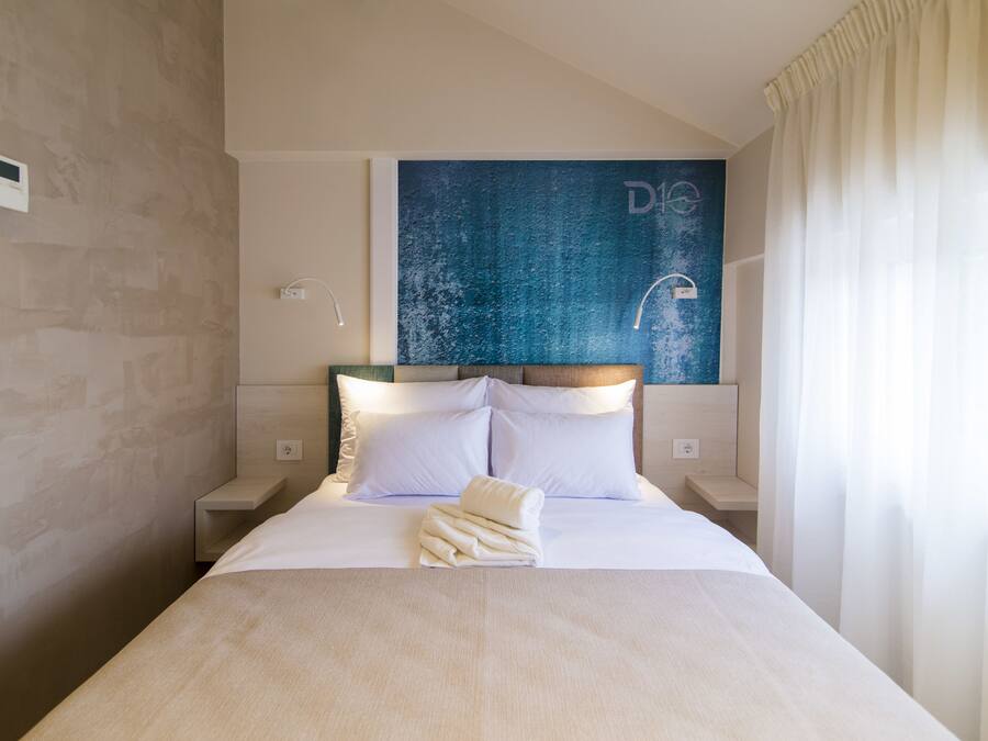 Quarto de hotel com uma cama grande, duas mesas de cabeceira, uma obra de arte na parede e uma janela com cortinas.