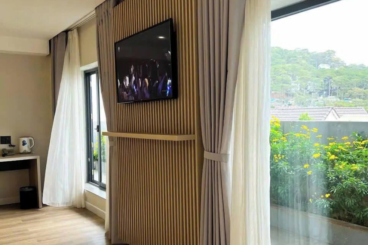 Quarto de hotel moderno com uma janela ampla, uma televisão de tela plana fixada em um painel de madeira e piso de madeira.