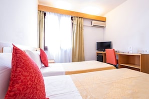 Quarto de hotel com duas camas, uma escrivaninha, uma televisão e aparelho de ar condicionado.