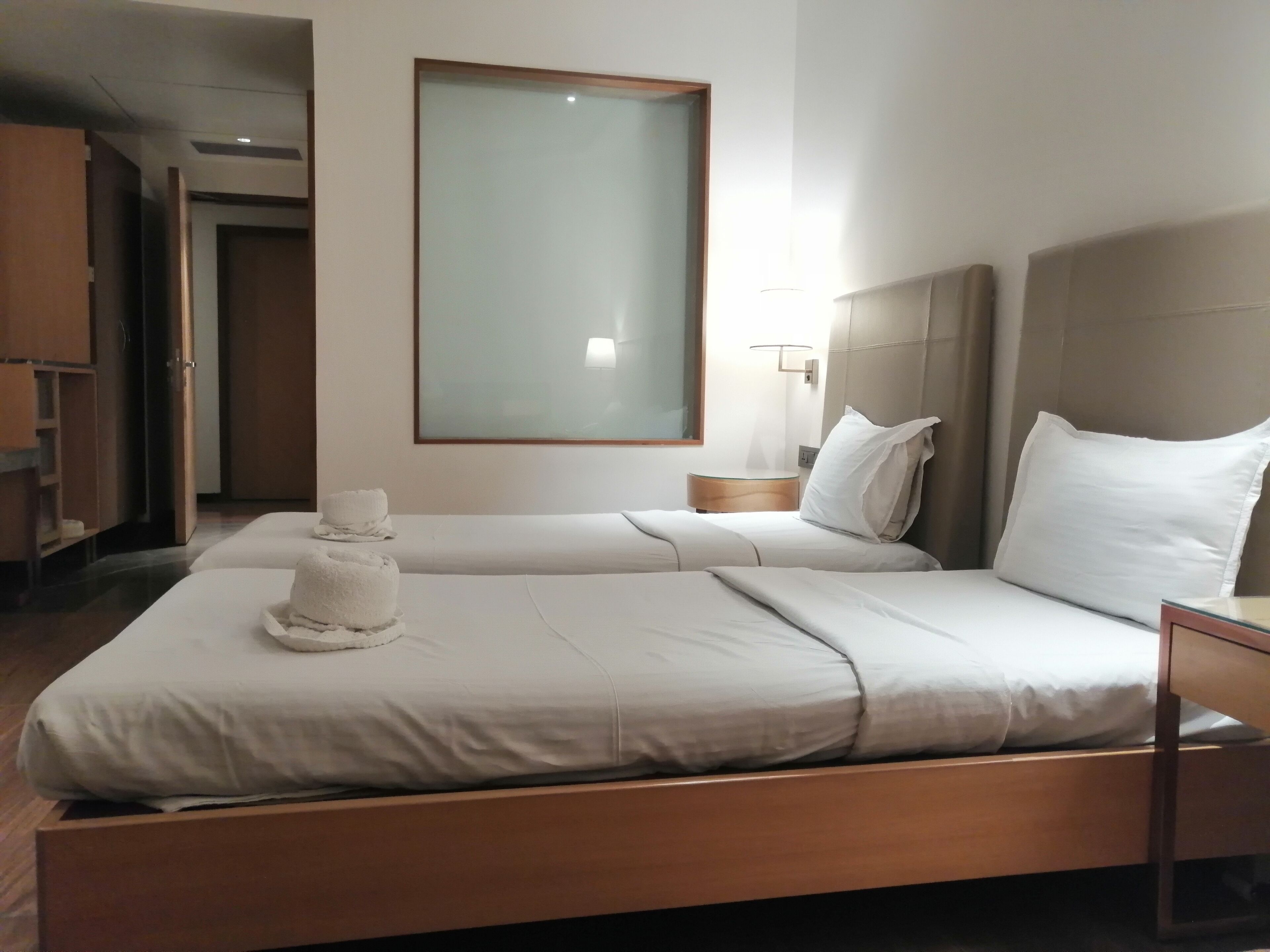 Quarto de hotel com duas camas, um espelho grande e uma mesa de cabeceira com abajur.