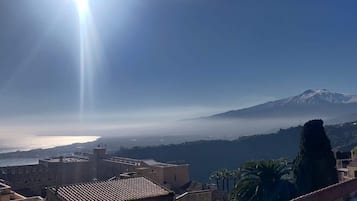 Uma cidade costeira com uma montanha imponente ao fundo, edifícios com telhados em terracota e uma vista clara do mar.