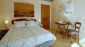 Quarto com uma cama grande, uma porta de madeira, uma pequena mesa com cadeira e uma obra de arte na parede.