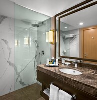 Um banheiro moderno com chuveiro envidraçado, paredes de mármore, um espelho grande e toucador de mármore com amenities.