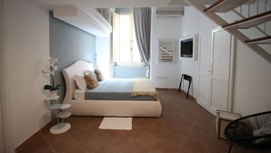 Quarto com cama, uma mesinha, cadeira, televisão e escada.
