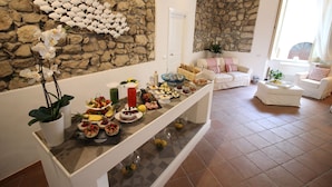 Uma mesa de buffet com diversos pratos, uma parede de pedra e uma área de estar com mobiliário branco.