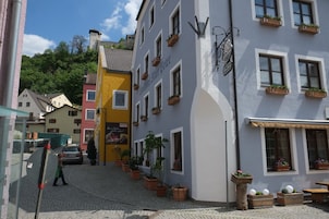 Uma rua de paralelepípedos com um edifício amarelo, um edifício branco com caixas de flores e uma placa indicando um restaurante.
