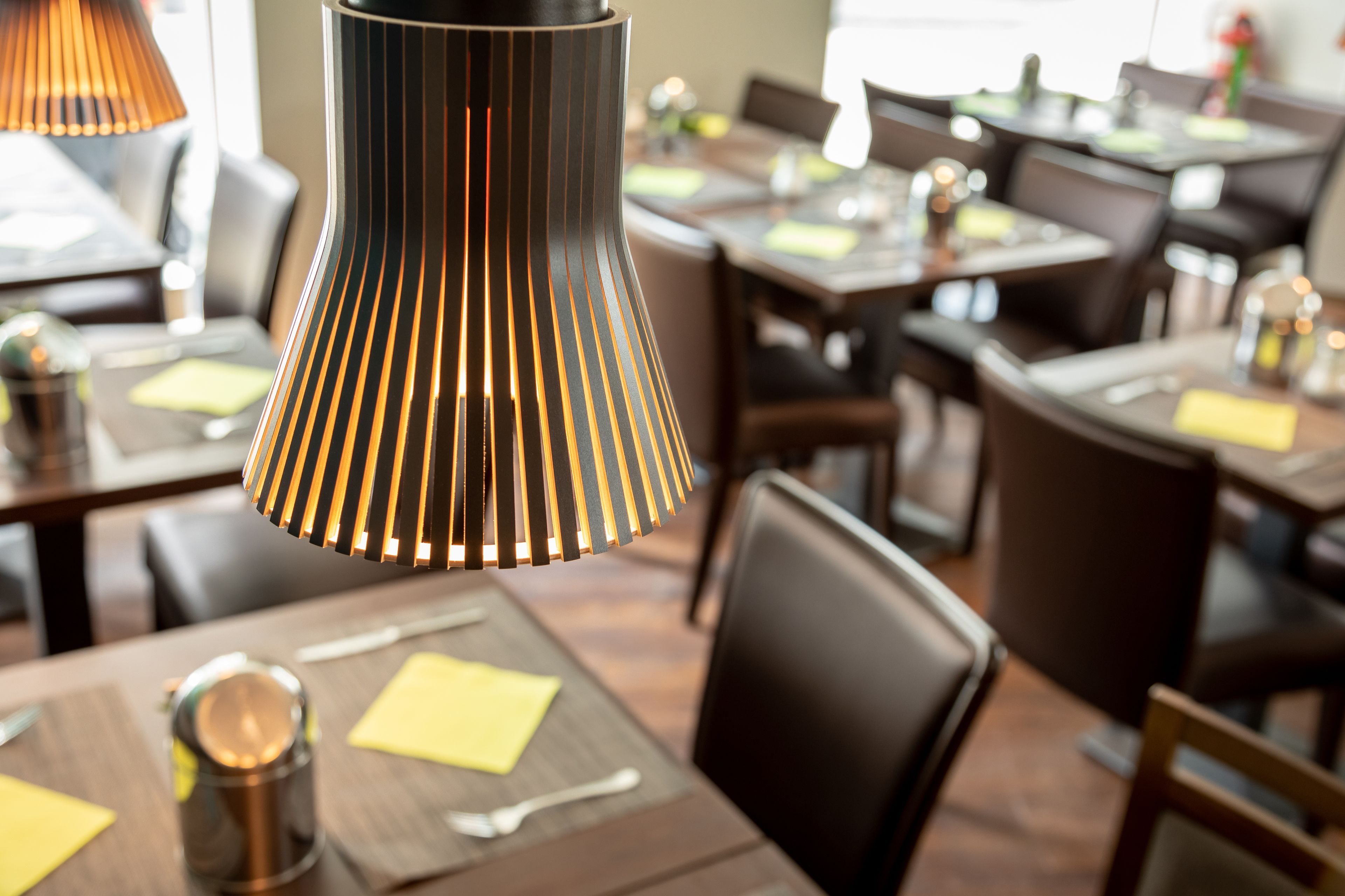 Interior de restaurante com mesas preparadas para refeições, uma luminária pendente e uma estética de design moderna.
