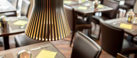 Interior de restaurante com mesas preparadas para refeições, uma luminária pendente e uma estética de design moderna.